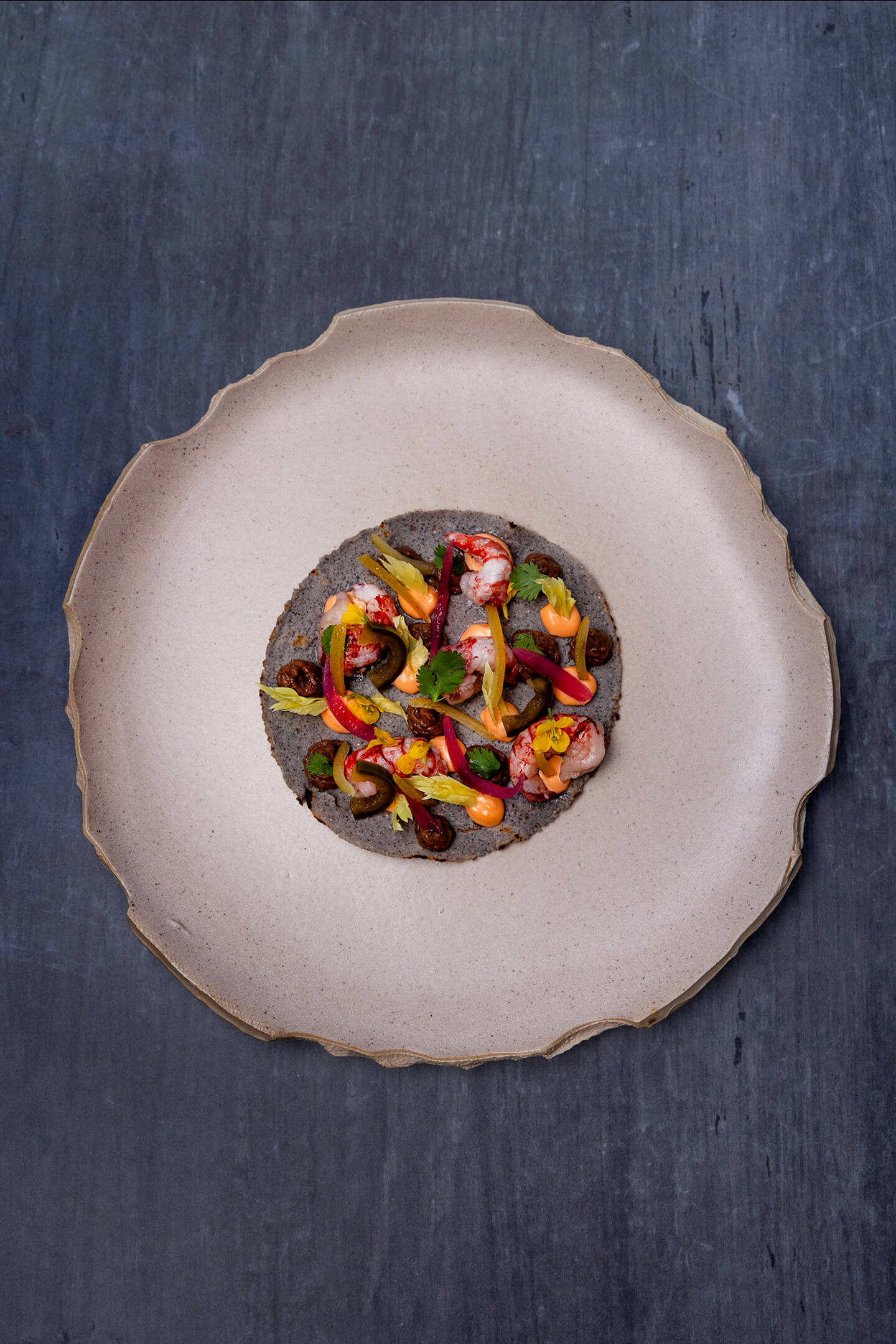 Sous vide cooked crayfish with black beans and pickles on a blue corn ...